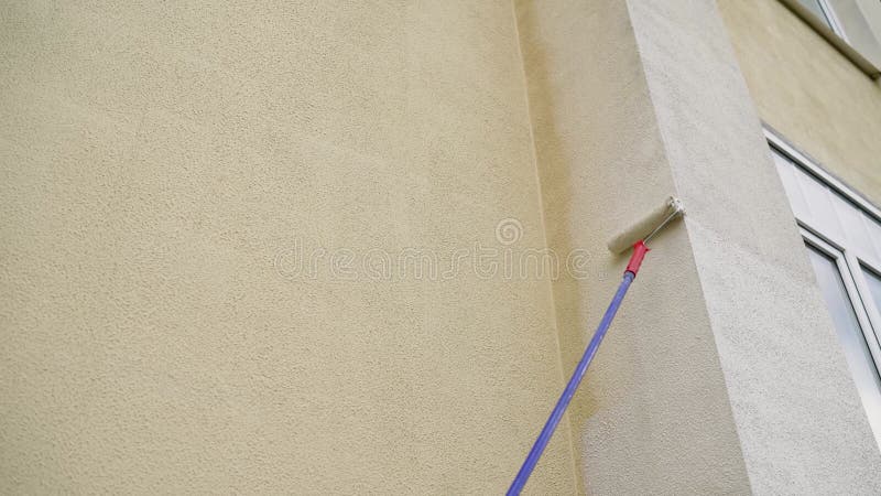 Construction Worker is Painting a Building Using a Paint Roller on a ...