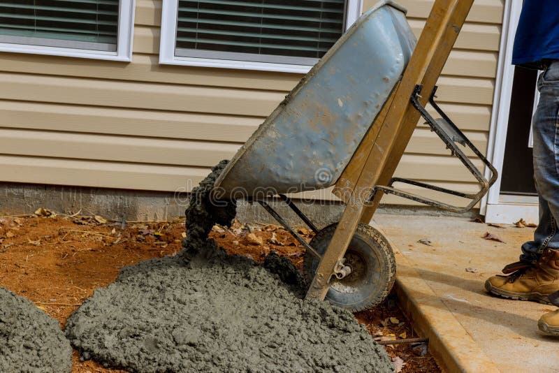 A Construction Worker Pours Cement from a Wheelbarrow on the Side of ...