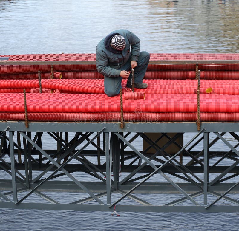 Construction Worker with Red Pipes on a Metal Structure Above Water ...