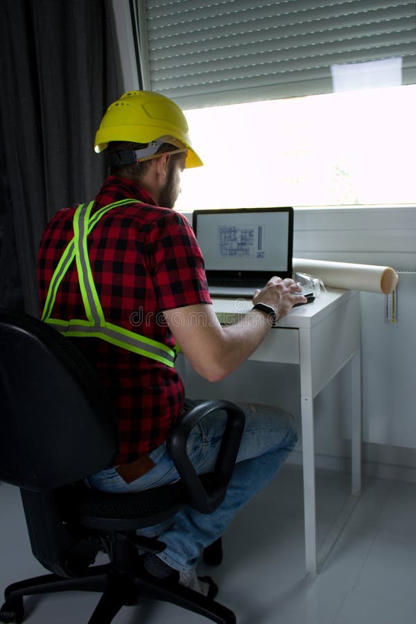 Construction Worker is Sitting at His Desk at the Computer, Looking at ...