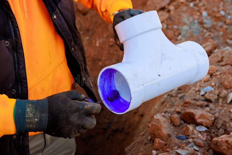 Worker Applying Adhesive To a White PVC Pipe Fitting in a Construction ...