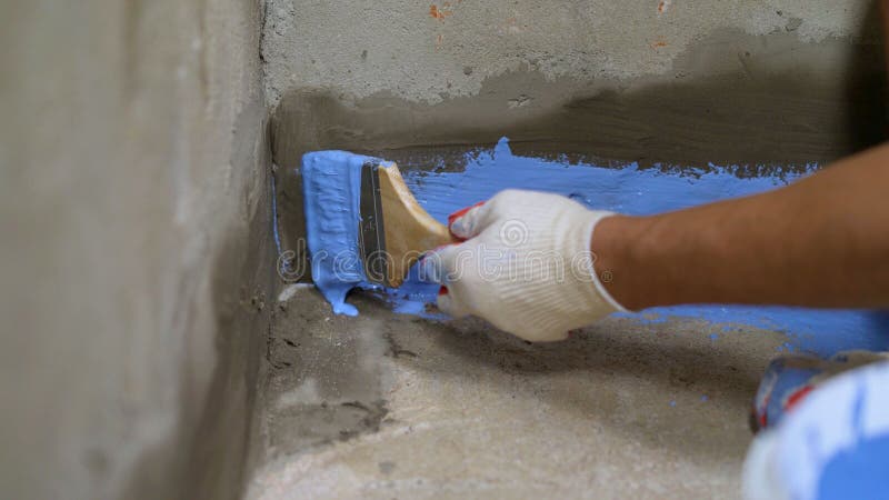Construction worker applying blue waterproofing paint on concrete wall ...