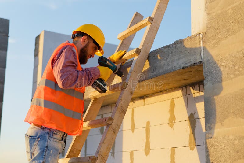 Construction Worker Using Cordless Drill on Wooden Ladder at Building ...