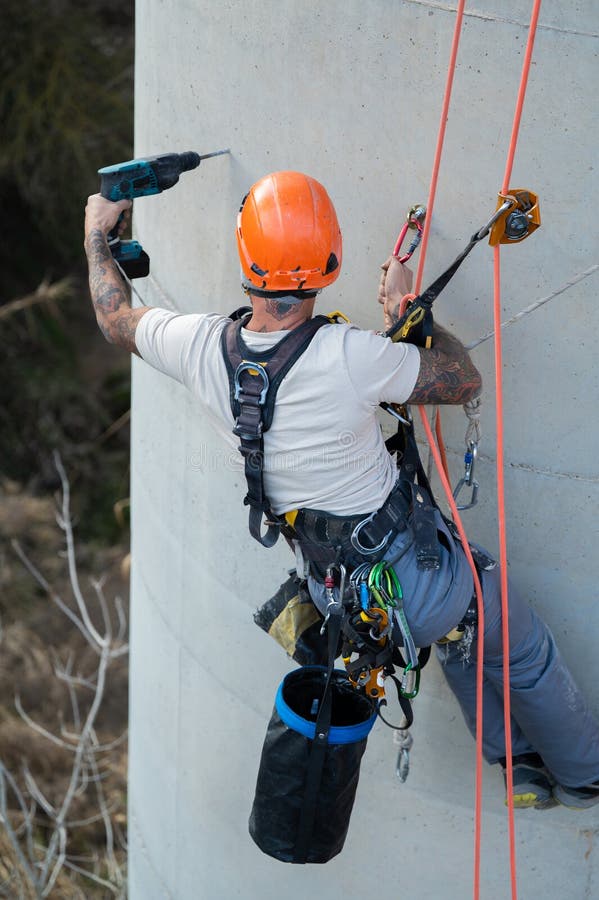 Construction Worker Using Drill while Hanging on Ropes on Concrete Wall ...