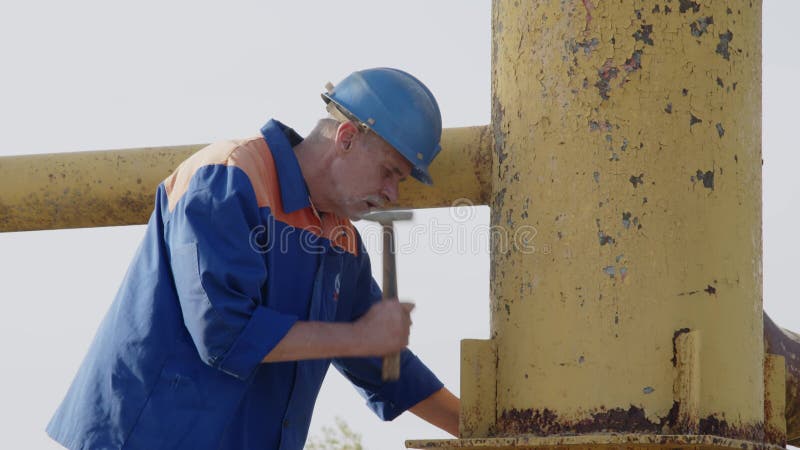 Construction Worker is Using a Hammer To Work on an Industrial Pipe ...