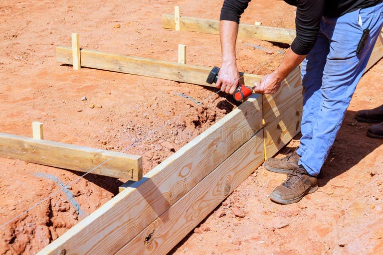 Construction Worker Using a Power Tool To Secure Wooden Beams on a Building Site during Daylight ...