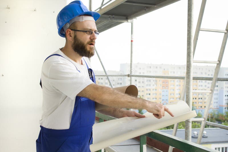 Construction Worker in a Work Outfit and in a Helmet Stands at a High ...