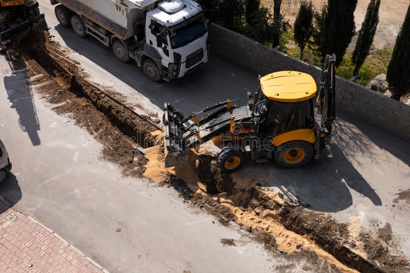 Construction Workers Operate Machinery in a Roadside Excavation Project ...