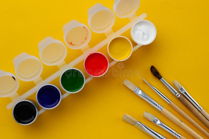 Containers with Multi-colored Paint on a Yellow Background and Brushes ...