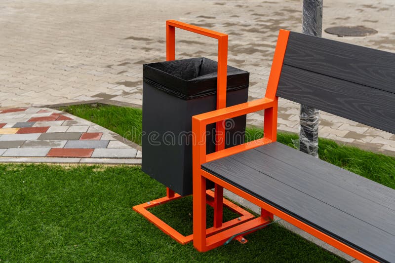A Contemporary Garbage Container is Mounted Alongside a Park Bench ...