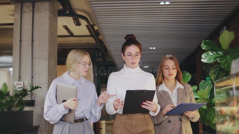 Three Professional Women Walk through the Office Collaborate Using Tablets and Documents To ...