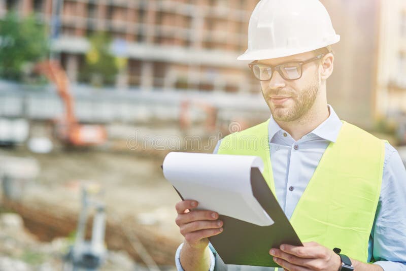 Young Civil Engineer Wearing Helmet Writing Report while Standing at ...