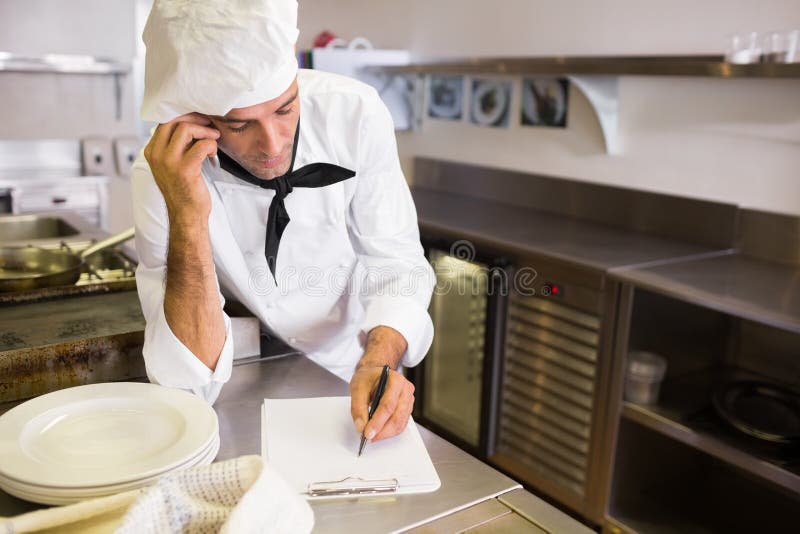 Cook Writing on Clipboard while Using Cellphone in Kitchen Stock Image ...