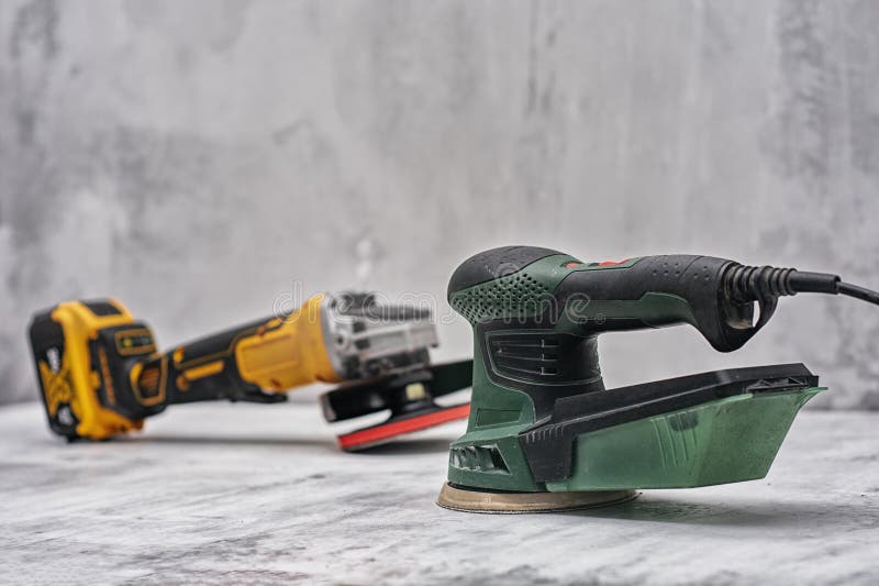 Cordless Grinder and a Sander Rest on a Concrete Surface Against a ...