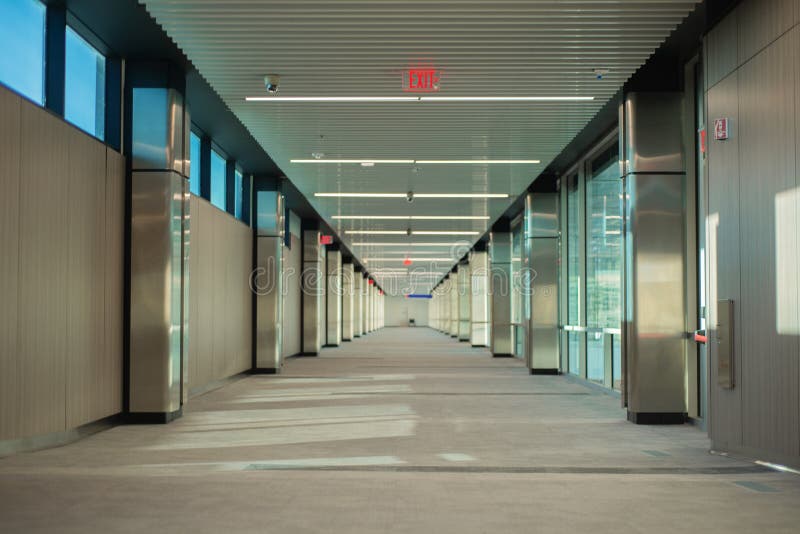 Corridor of Empty Building with Exit Signs Lit in Red and Windows on ...