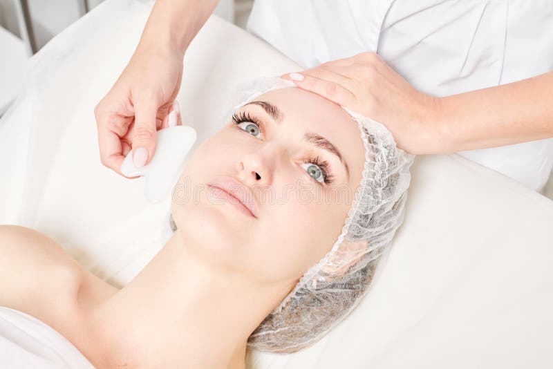 Cosmetologist Making Facial Massage With Gua Sha Stone Of Woman Face