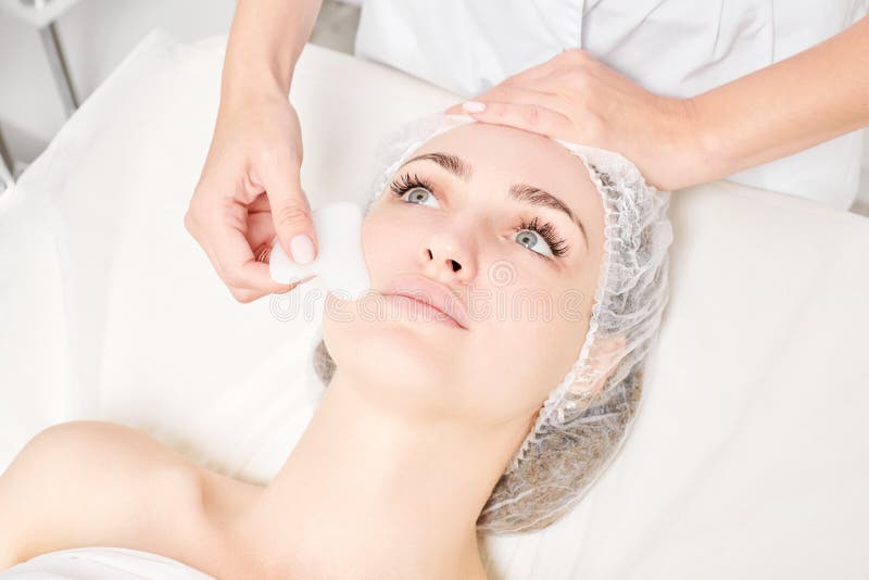 Cosmetologist Making Facial Massage With Gua Sha Stone Of Woman Face