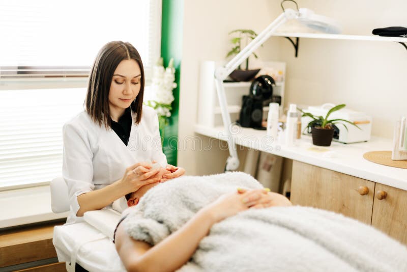 A Cosmetologist Massages The Skin Of A Young Woman With A Gouache