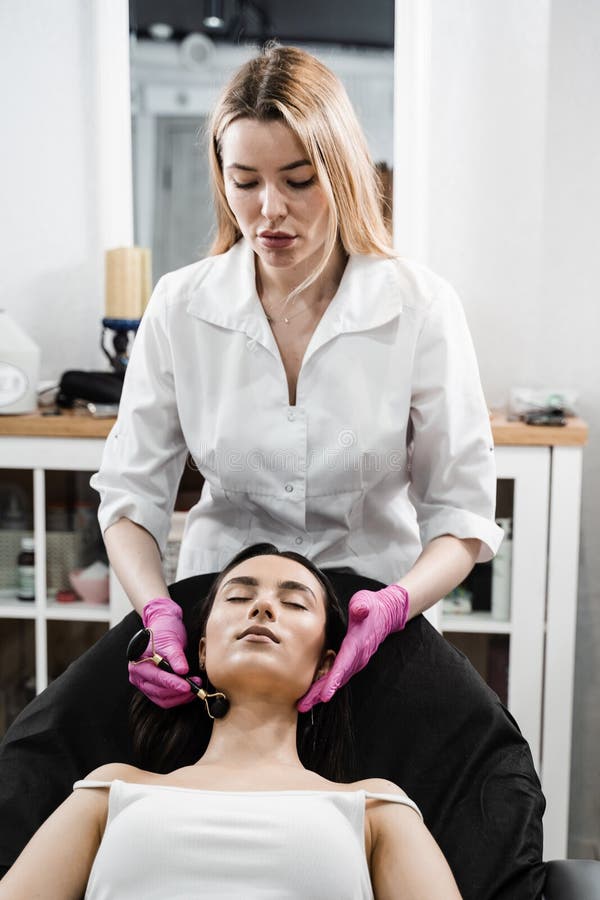 Cosmetologist Using Stone Roller For Face Massage For Girl Patient