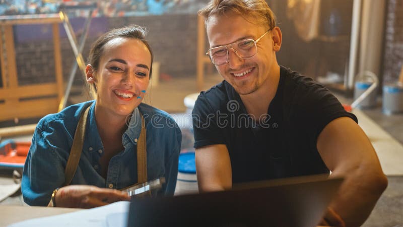 Couple of Artists Sitting in Their Studio Use Laptop Computer, Working ...