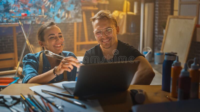 Couple of Artists Sitting in Their Studio Use Laptop Computer, Working ...