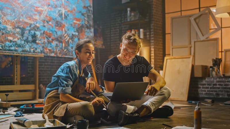 Couple of Artists Sitting in Their Studio Use Laptop Computer, Working ...