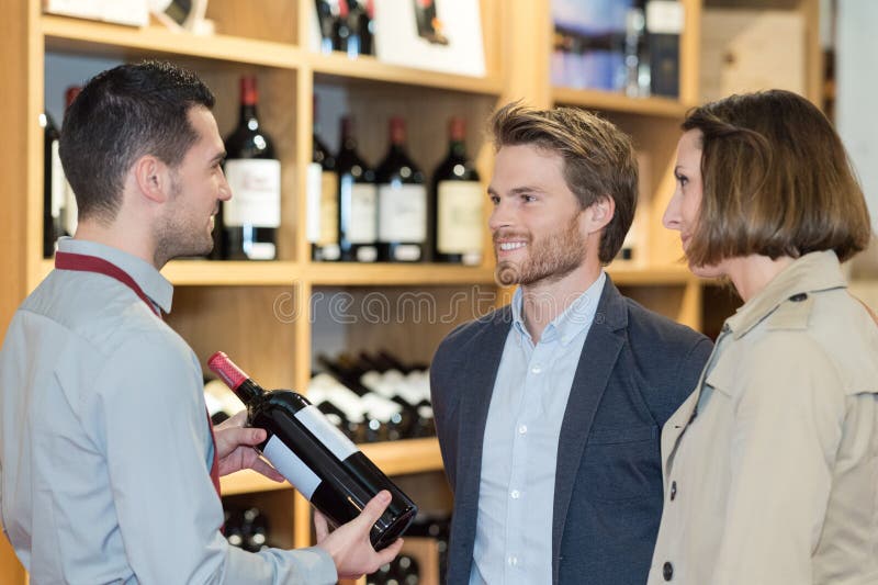 Couple Choosing Wine with Sales Assistant in Wine Shop Stock Photo ...