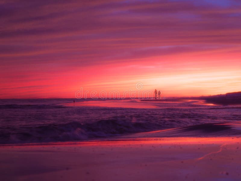 A Couple in the Distance Walks Down the Beach at Sunset Stock Photo ...