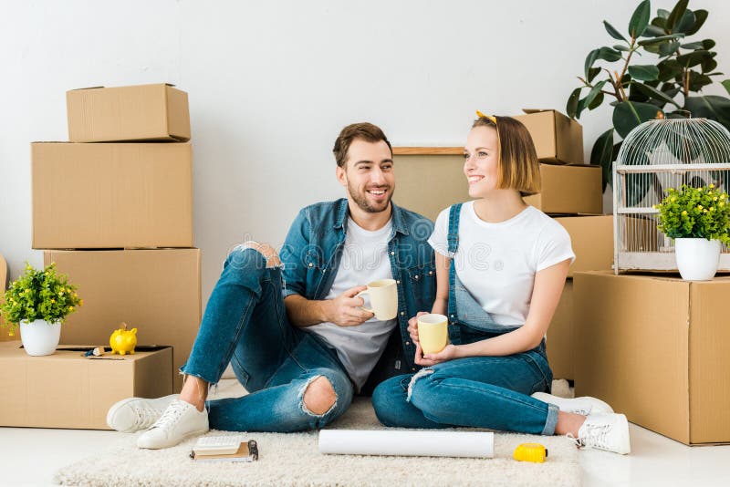 Couple Drinking Coffee While Sitting On Floor Near Cardboard Boxes