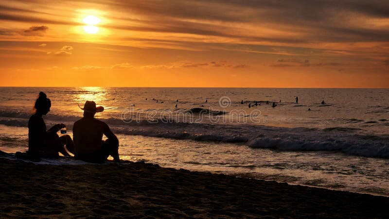 Couple Enjoys Sunset on the Beach while Surfers Ride Waves in the ...
