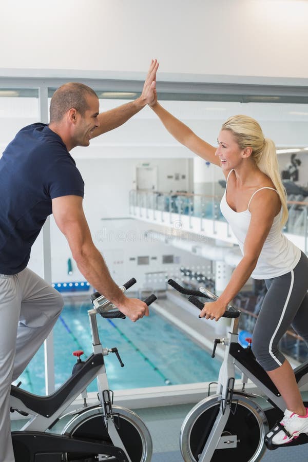 Couple Giving High Five while Working on Exercise Bikes at Gym Stock ...