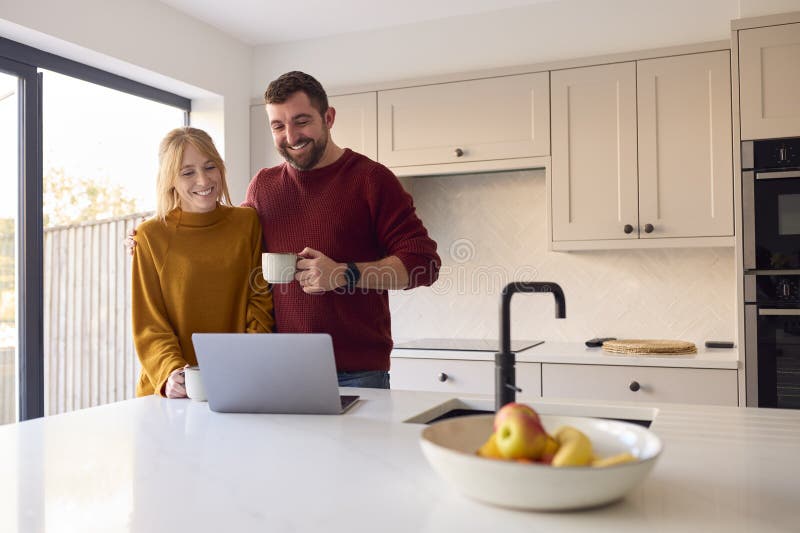 Couple at Home Looking at Laptop on Counter in Kitchen Together Stock ...