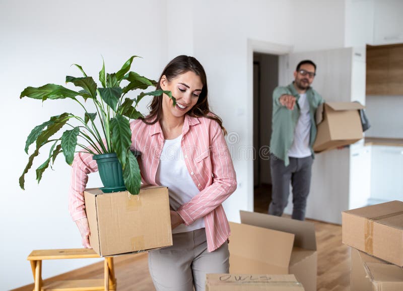 Couple Moving In In Their New Apartment And Carrying Cardboard Boxes
