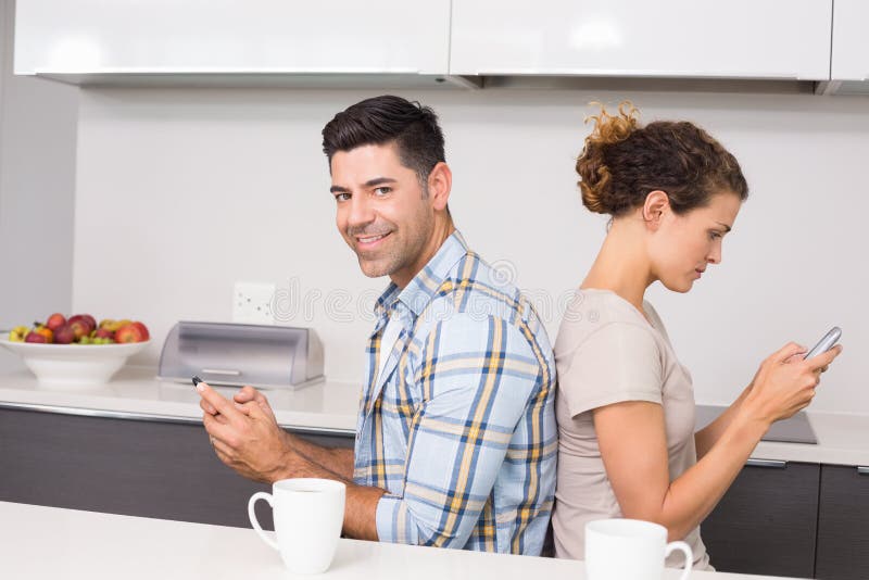 Couple Sitting Back To Back Texting with Man Smiling at Camera Stock ...