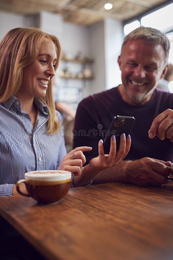 Couple Sitting at Table in Coffee Shop Looking at Mobile Phone Together ...