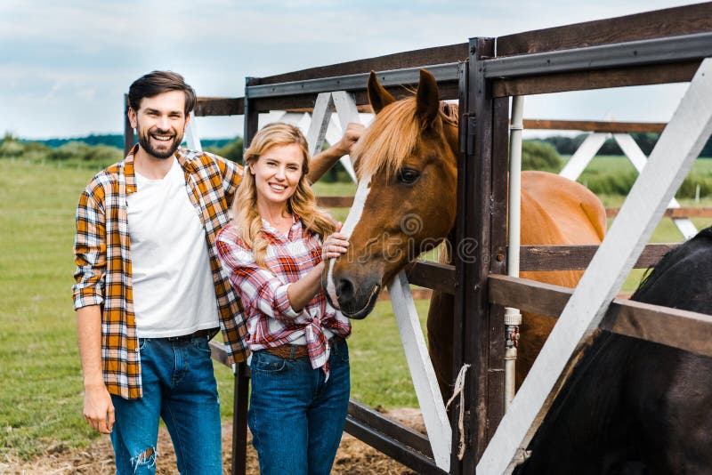 Couple of Smiling Ranchers Palming Horse in Stable and Looking Stock ...