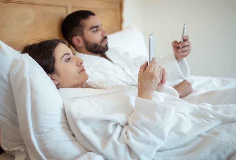 Couple Using Phones Texting Lying In Bed Wearing Bathrobes Indoors Stock Image Image Of Couple 7322