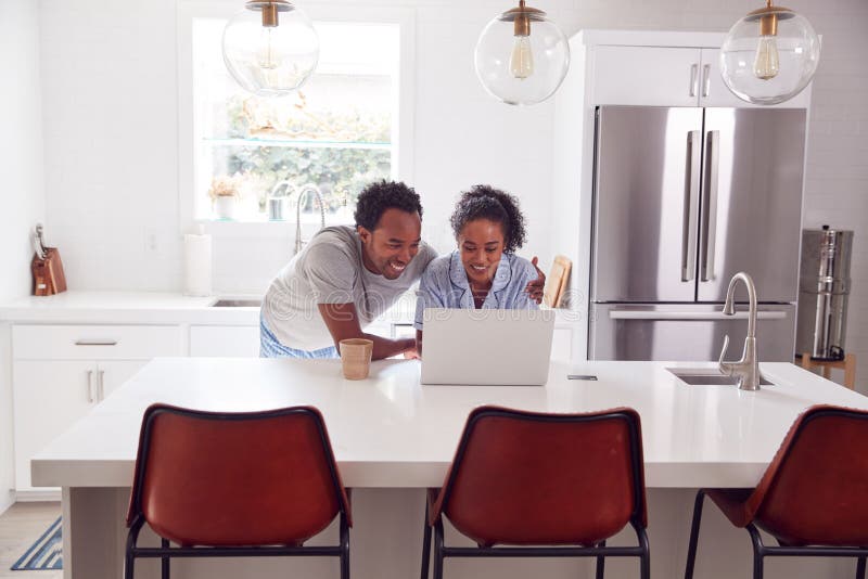 Couple Wearing Pyjamas Standing in Kitchen Working from Home on Laptop ...