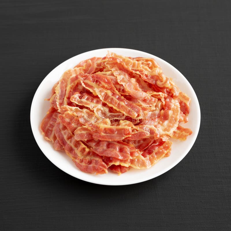 Crispy Fried Bacon on a White Plate on a Black Background, Side View ...