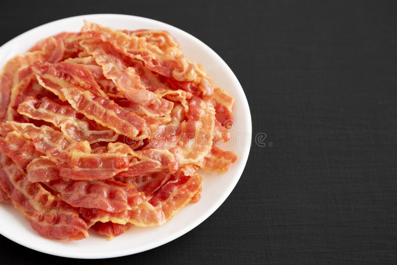Crispy Fried Bacon on a White Plate on a Black Surface, Side View Stock ...