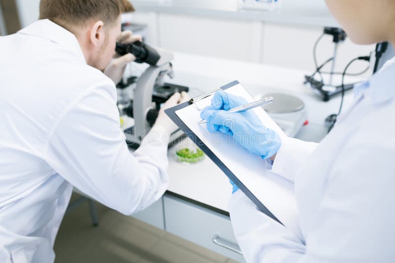 Scientists Writing Results of Research Under Microscope Stock Photo ...