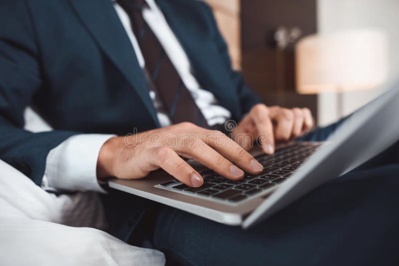 Cropped Shot of Businessman in Formal Suit Sitting on Bed and Using ... Cropped Shot of Businessman in Formal Suit Sitting on Bed and Using ...