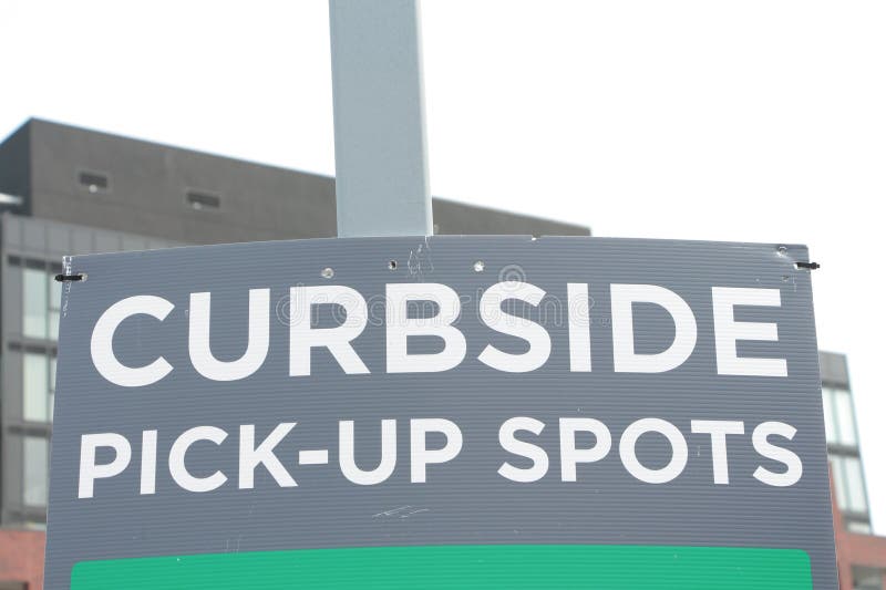 Curbside Pick Up Spots Sign on Post with Building and Sky in Background ...