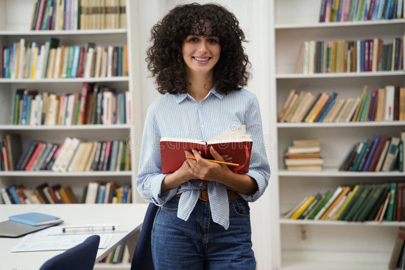 Curly-haired Woman Standing in the Library with a Book in Hands Stock ...