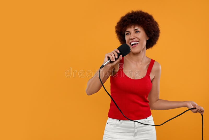 Curly Young Woman with Microphone Singing on Yellow Background, Space ...