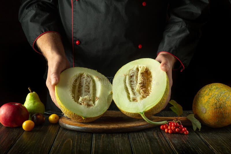 Cut Ripe Melon in the Hands of the Chef on the Kitchen Table. the ...