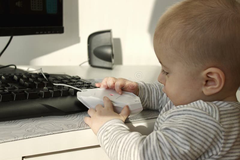 A Cute Baby Boy is Sitting at the Computer and Looks Attentively with ...