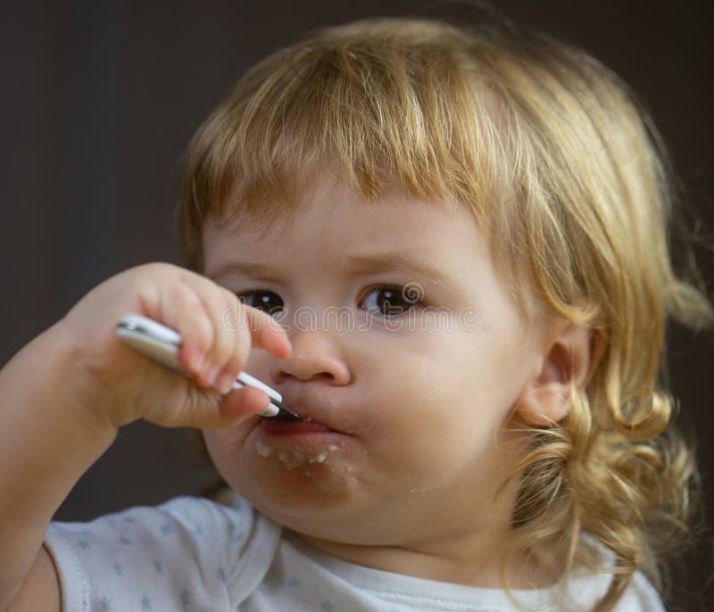 Cute Baby Face with a Spoon and a Plate in the Kitchen at Home. Stock ...