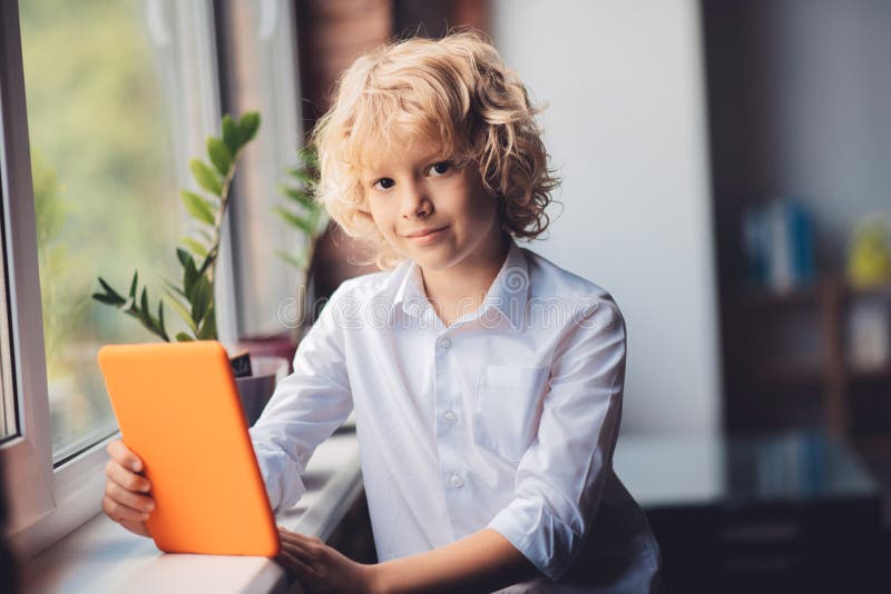 Cute Blonde Boy Holding a Tablet and Looking Thoughtful Stock Image ...