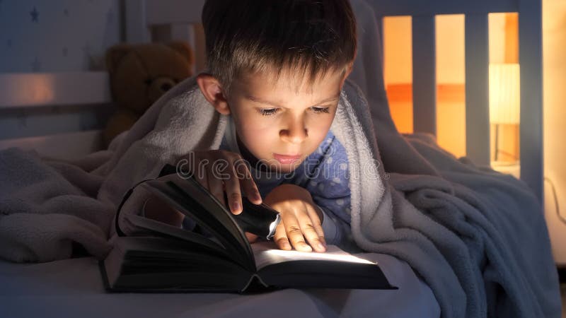 Cute Boy in Pajamas Reading a Book with Flashlight in Bed. Children ...